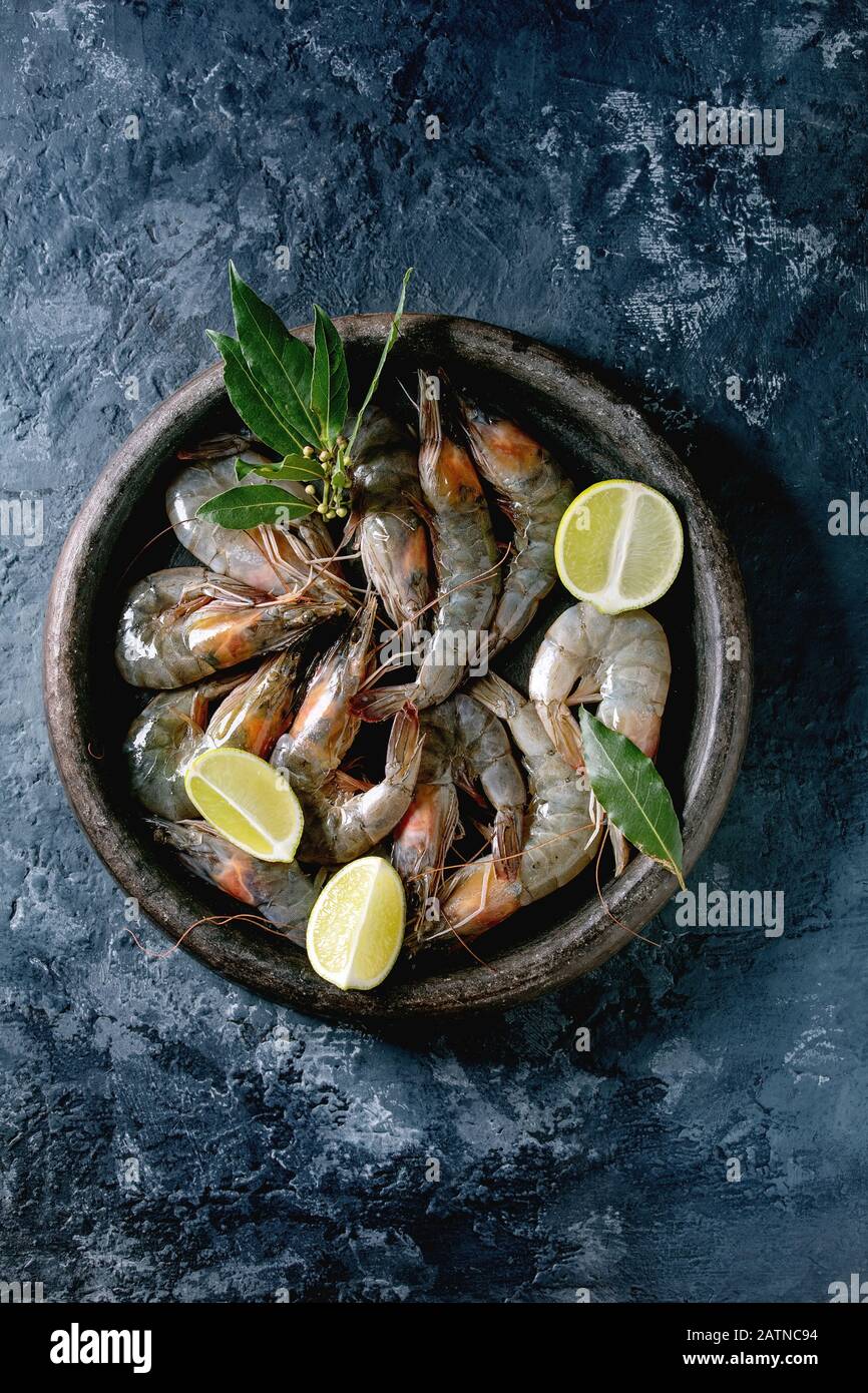 Raw uncooked prawns shrimp with lime and herbs in clay plate. Dark ...