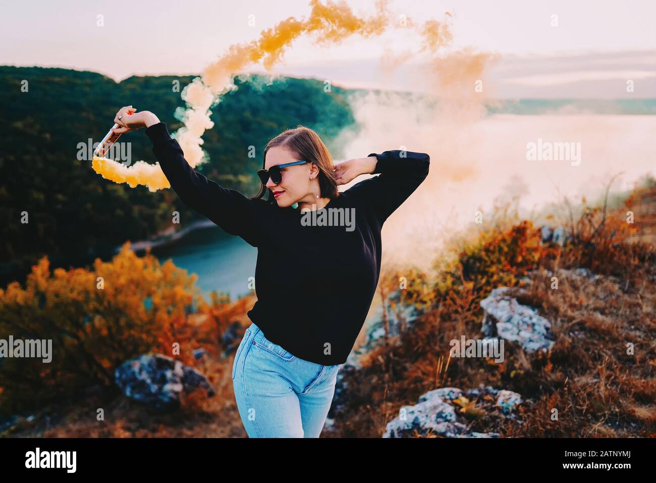 Young pretty woman with orange smoke bomb or grenade in dramatic moody ...
