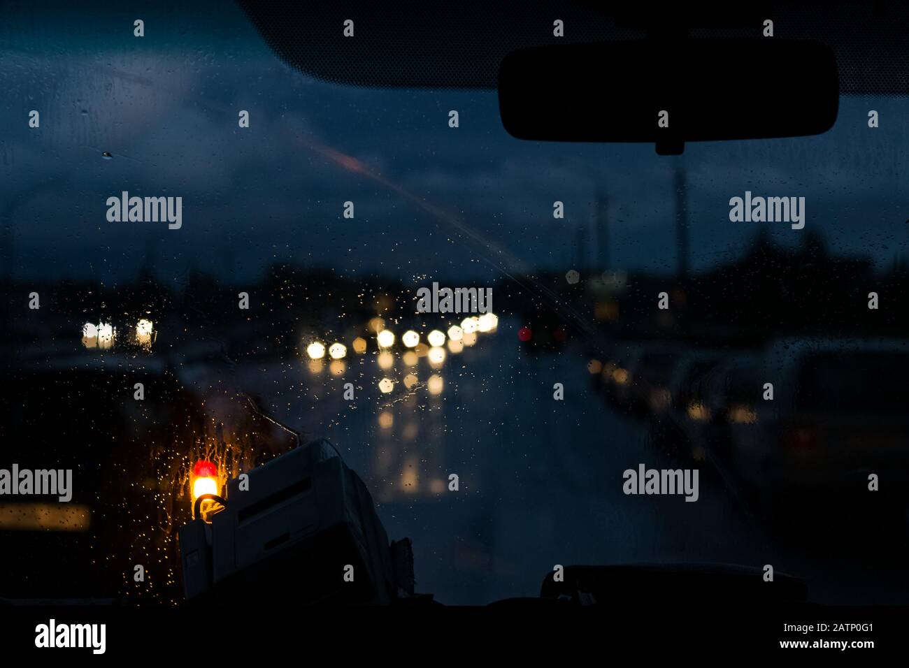 Car front window with raindrops and road with cars at night close up ...