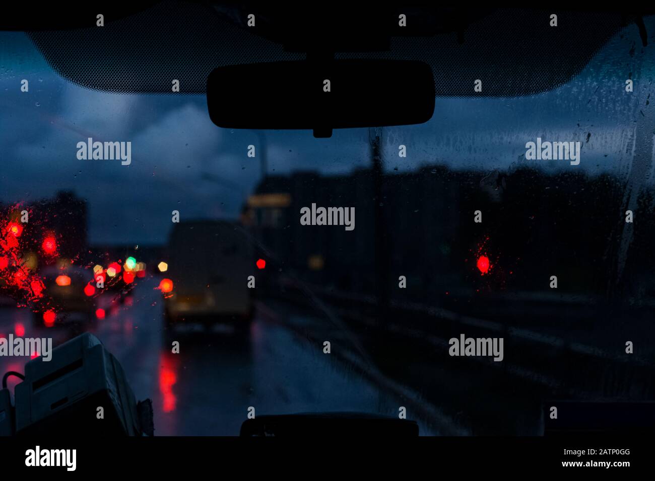 Car front window with raindrops and road with cars at night close up ...