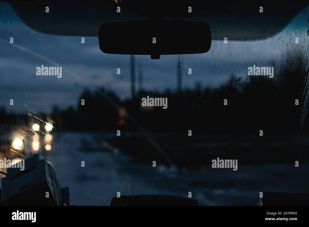 Car front window with raindrops and road with cars at night close up ...