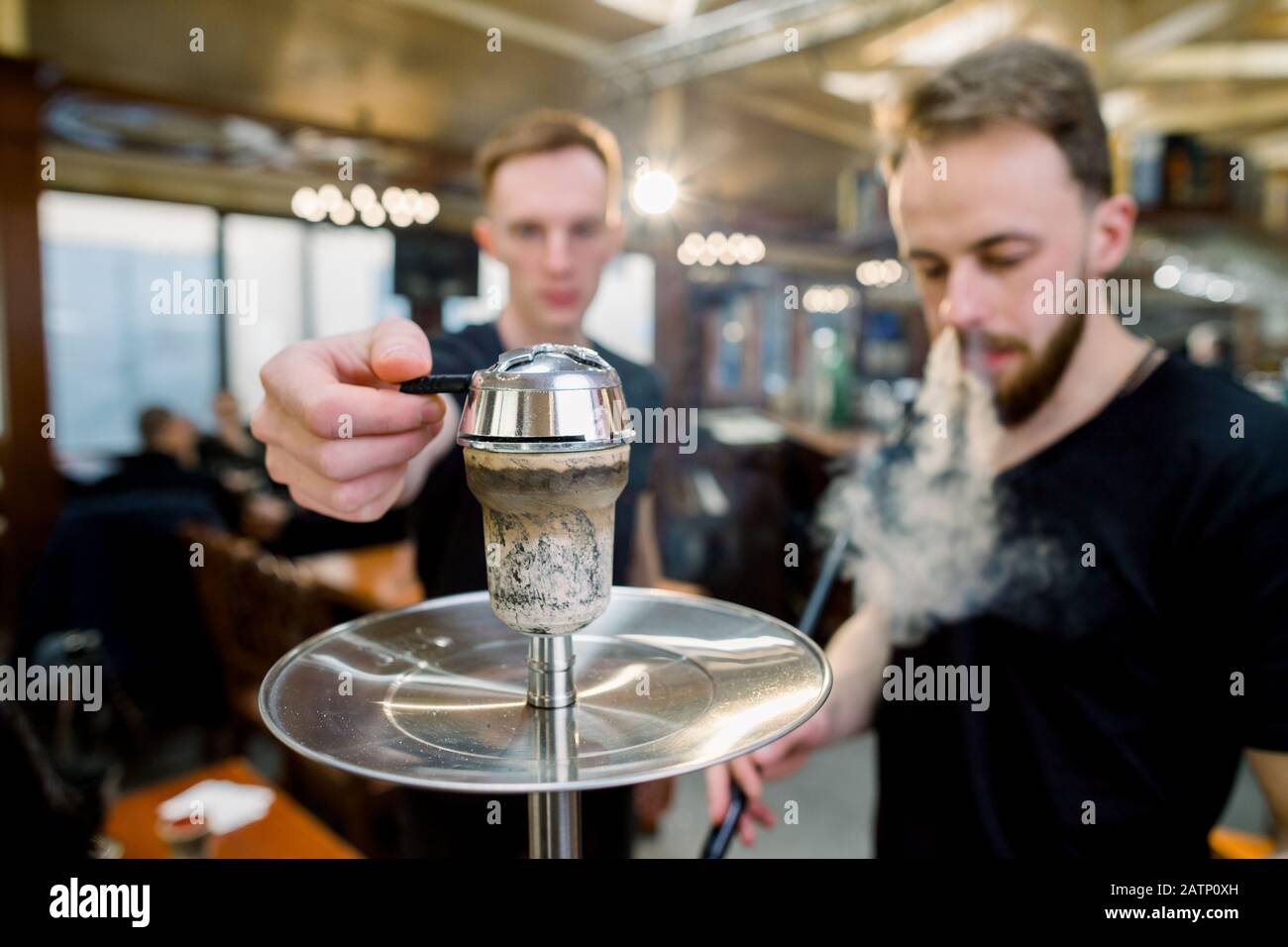 Two young boys preparing shisha by placing the charcoals on top. One ...