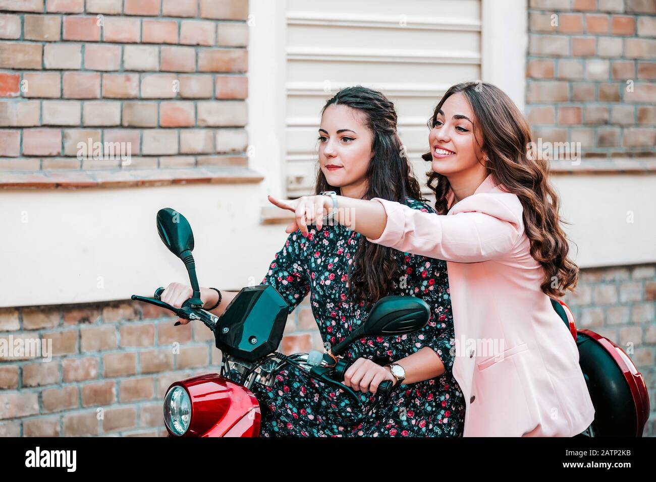 Two happy female friends riding on motorbike together through city ...