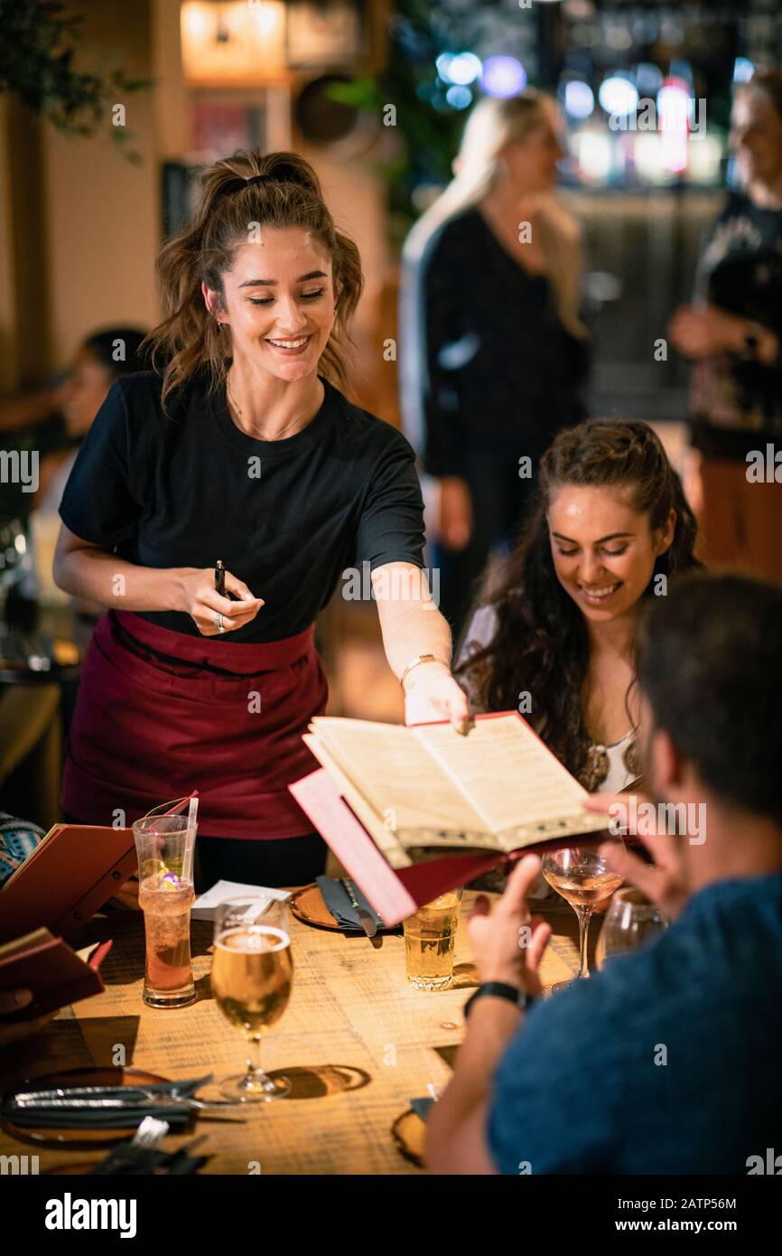 A waitress giving a menu to a customer, who is dining at a restaurant ...