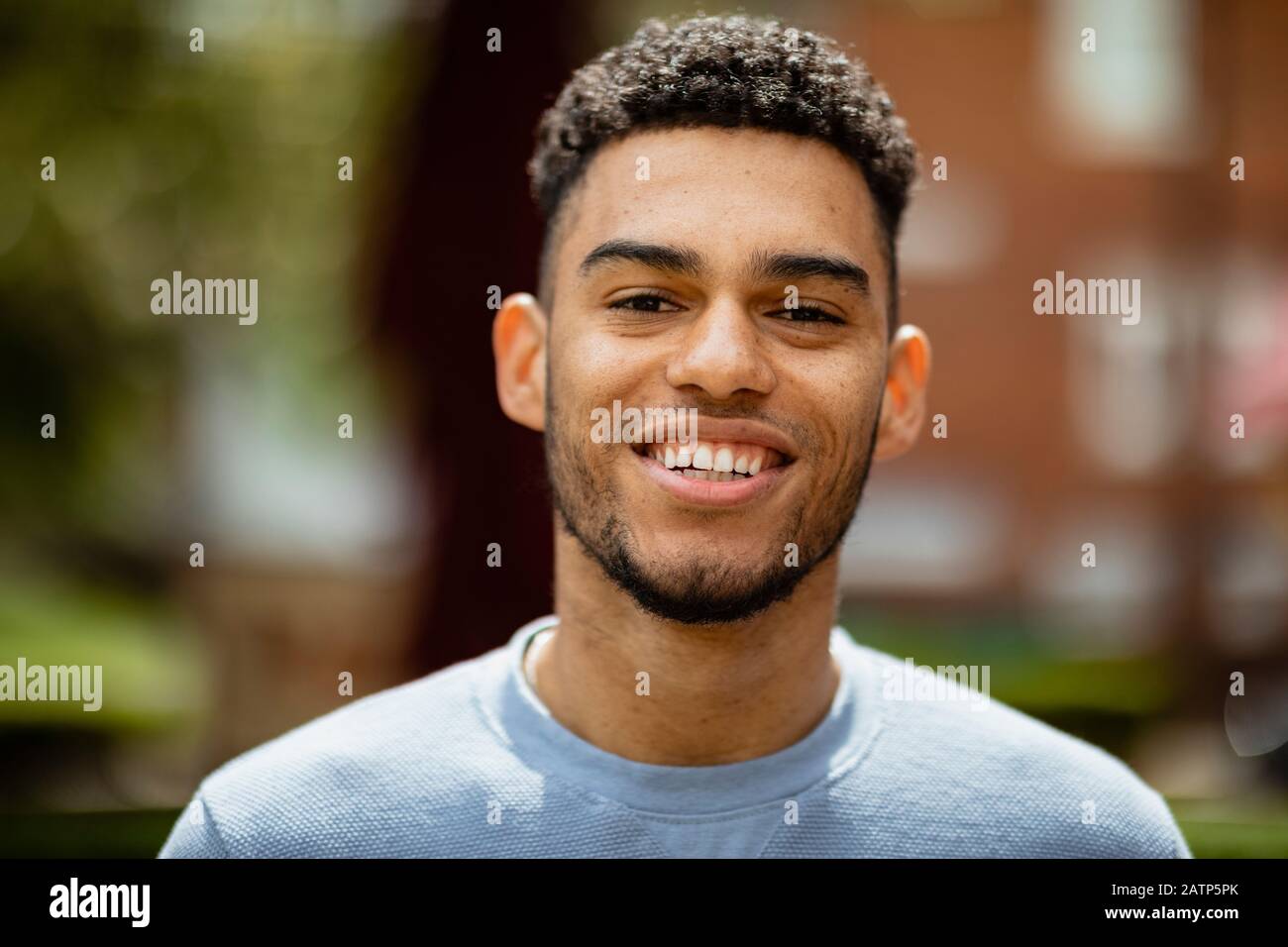 A portrait of a young adult man smiling while looking at the camera ...