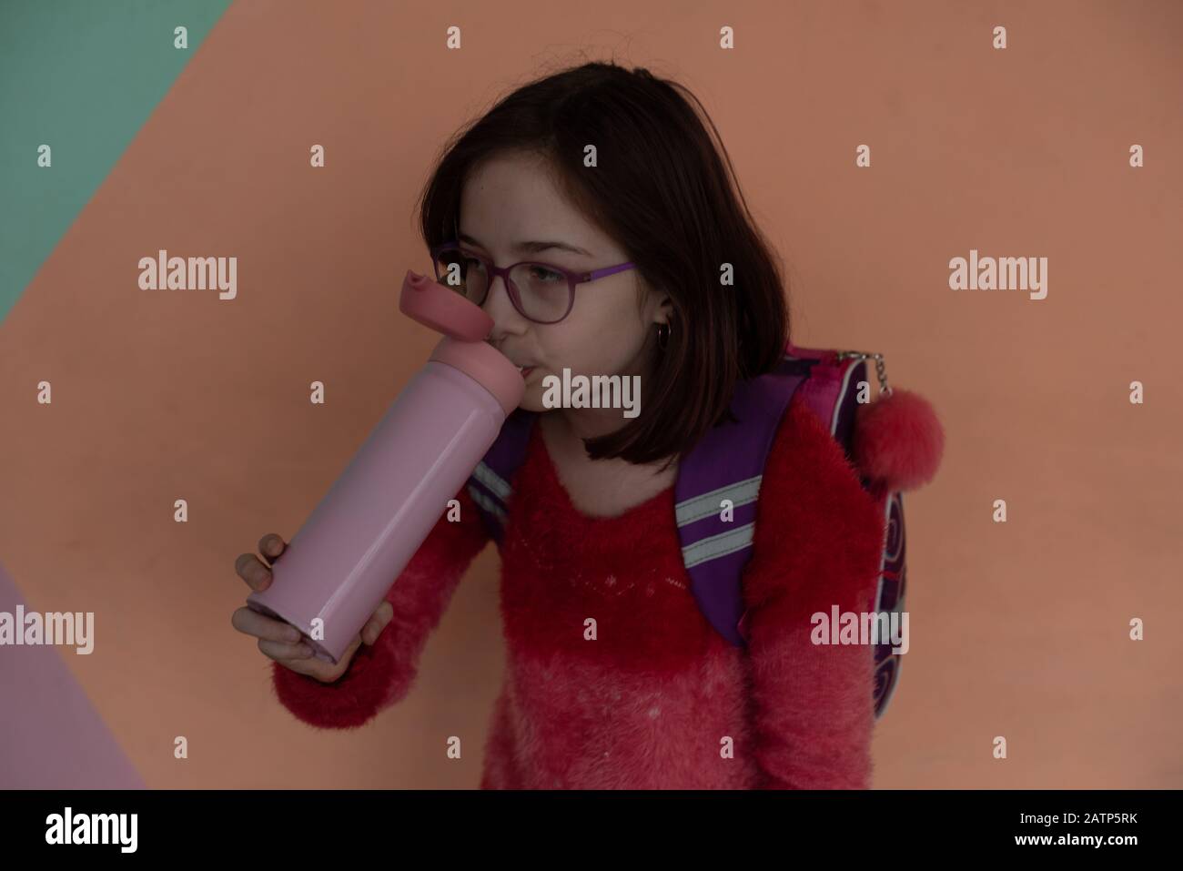 girl with cup. schoolgirl girl in glasses drinks water from a thermomug ...