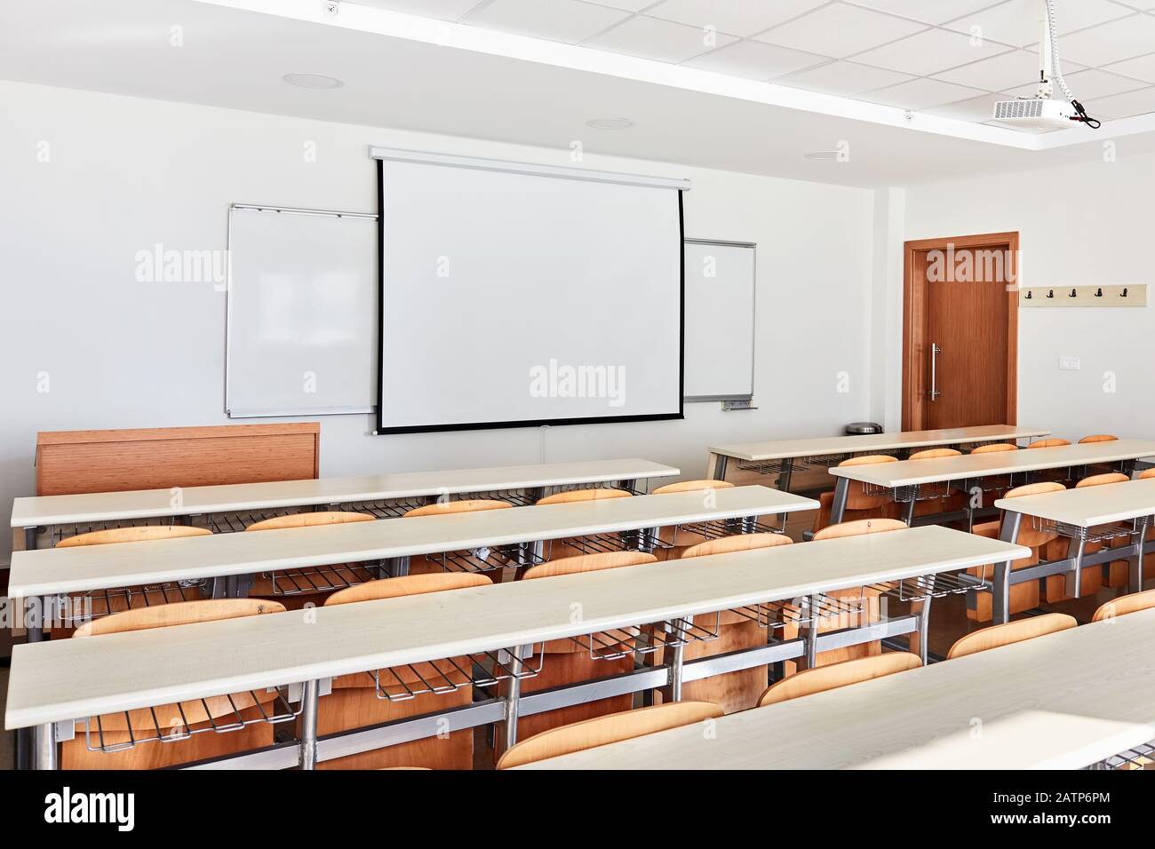 Classroom interior with white board, projection screen and wooden desks ...