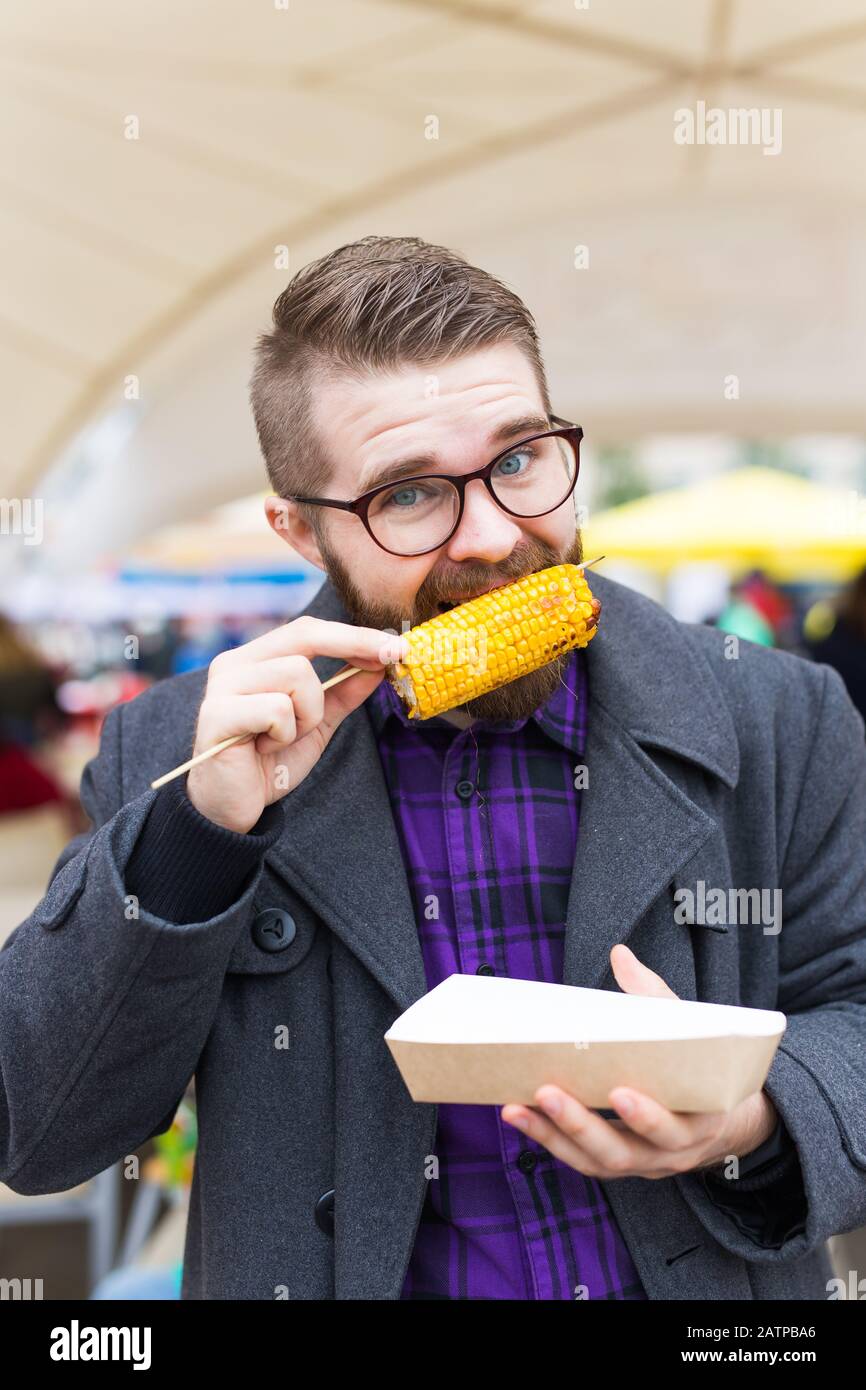 Handsome man eating street food corn at fast food festival Stock Photo ...
