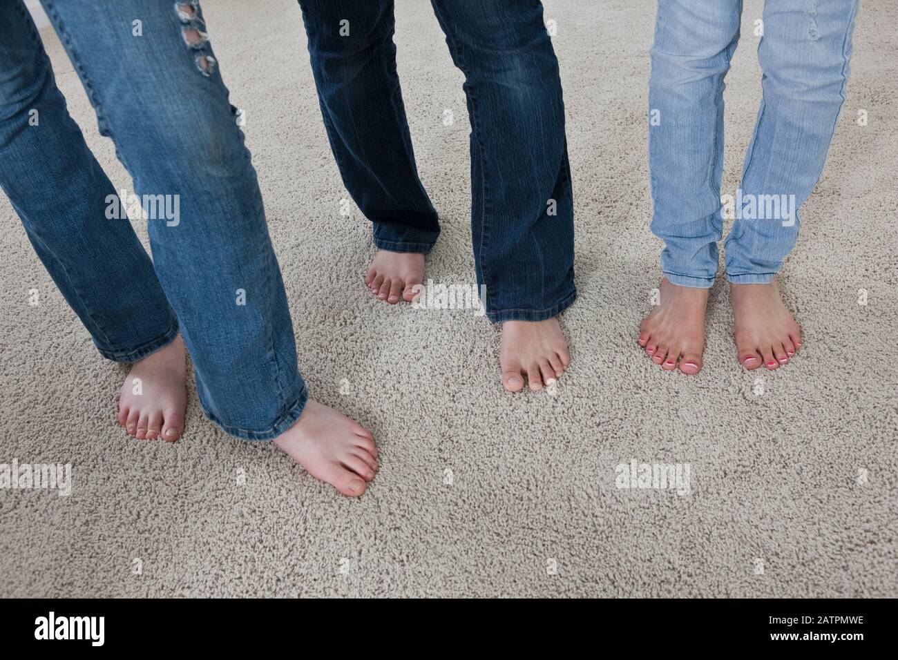Three sets of legs wearing denim jeans and bare feet standing on carpet ...