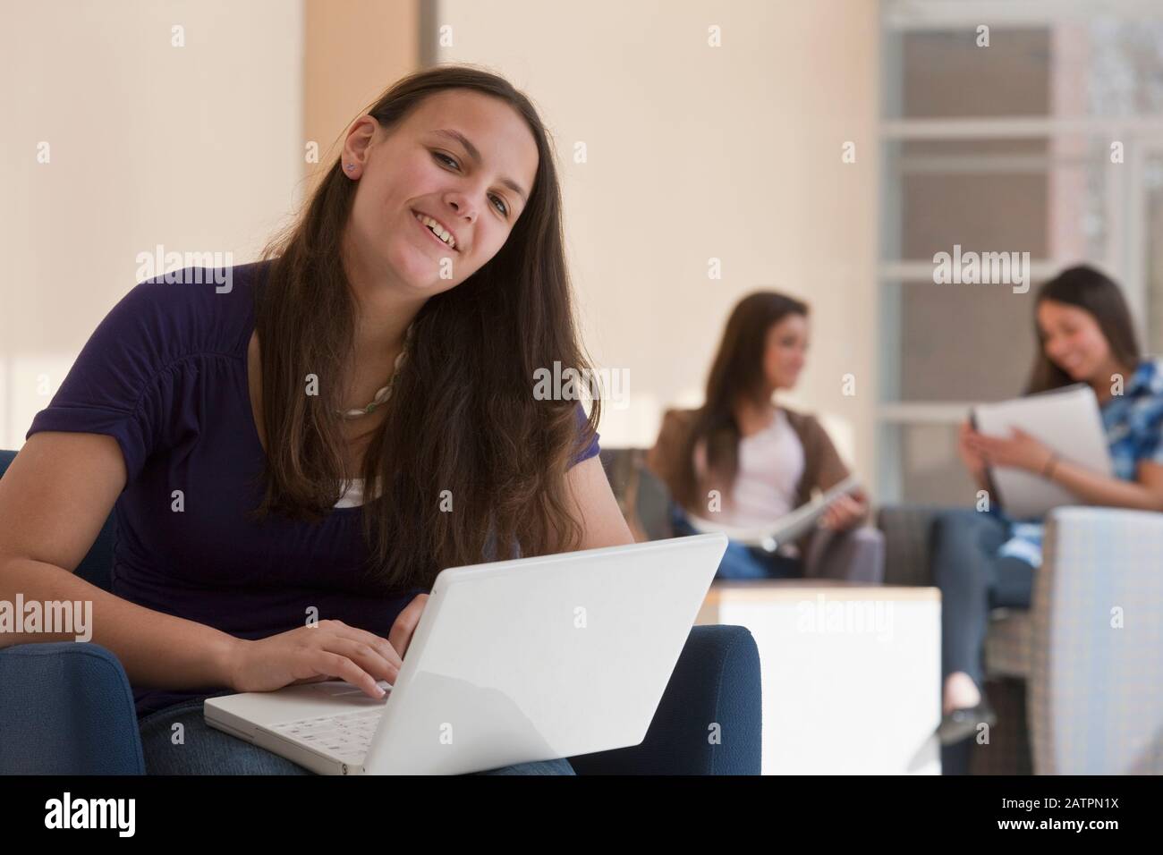 Teenage girl using laptop at school with two students looking at ...