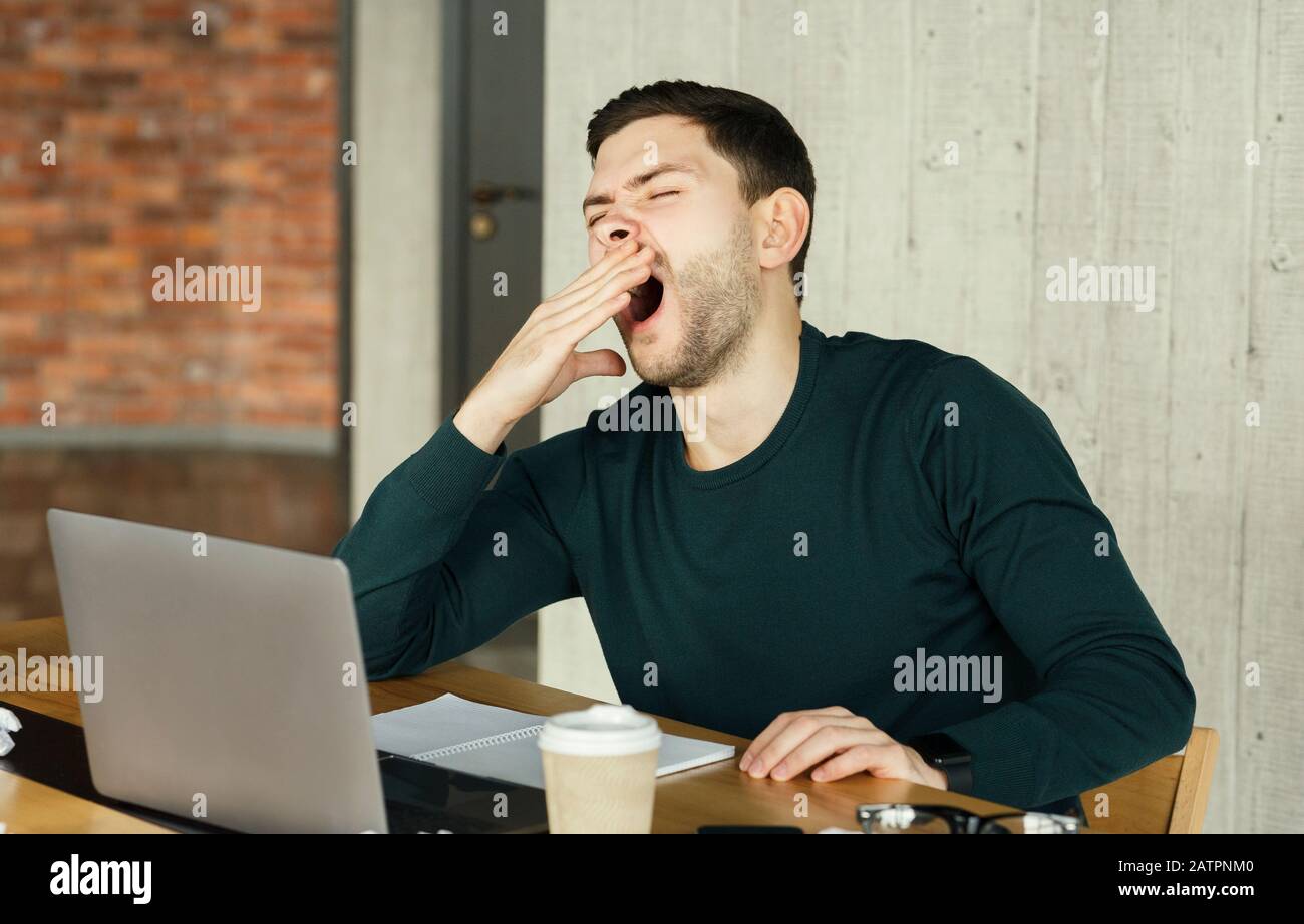 Tired Guy Yawning At Laptop Sitting At Workplace Indoor Stock Photo - Alamy
