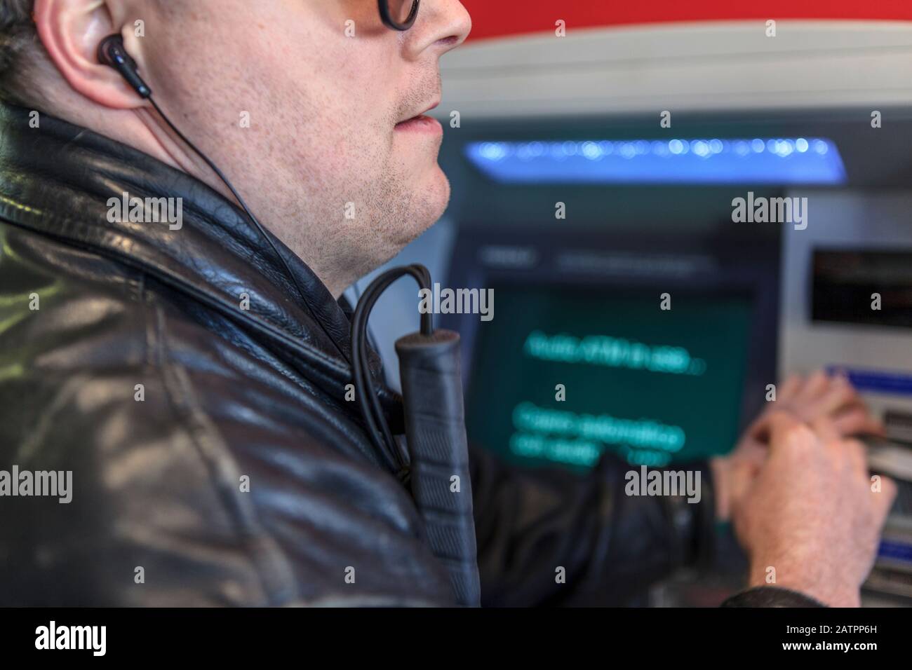 Man with visual impairment standing at a bank machine with a white cane ...