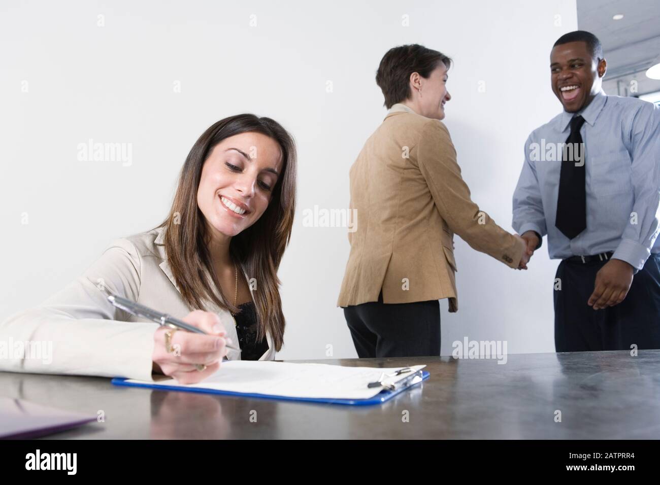 Business woman writing with business colleagues shaking hands in ...