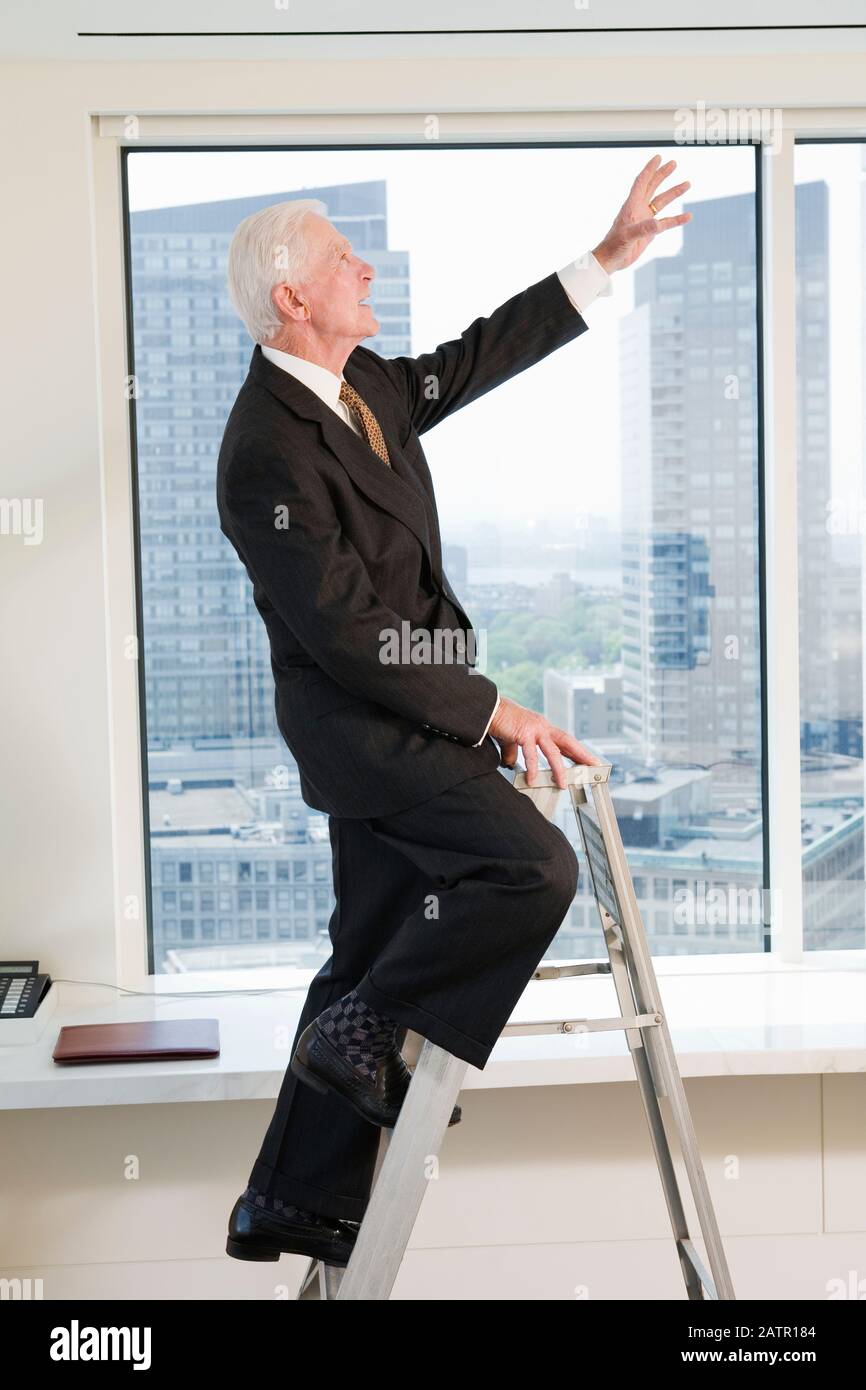 View of a businessman climbing a ladder in an office Stock Photo - Alamy