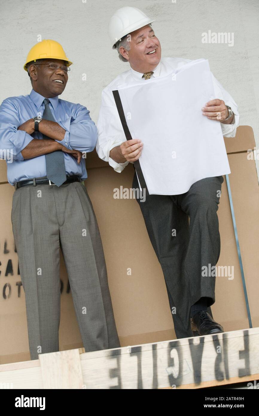 Two engineers leaning against a cardboard box and smiling Stock Photo ...