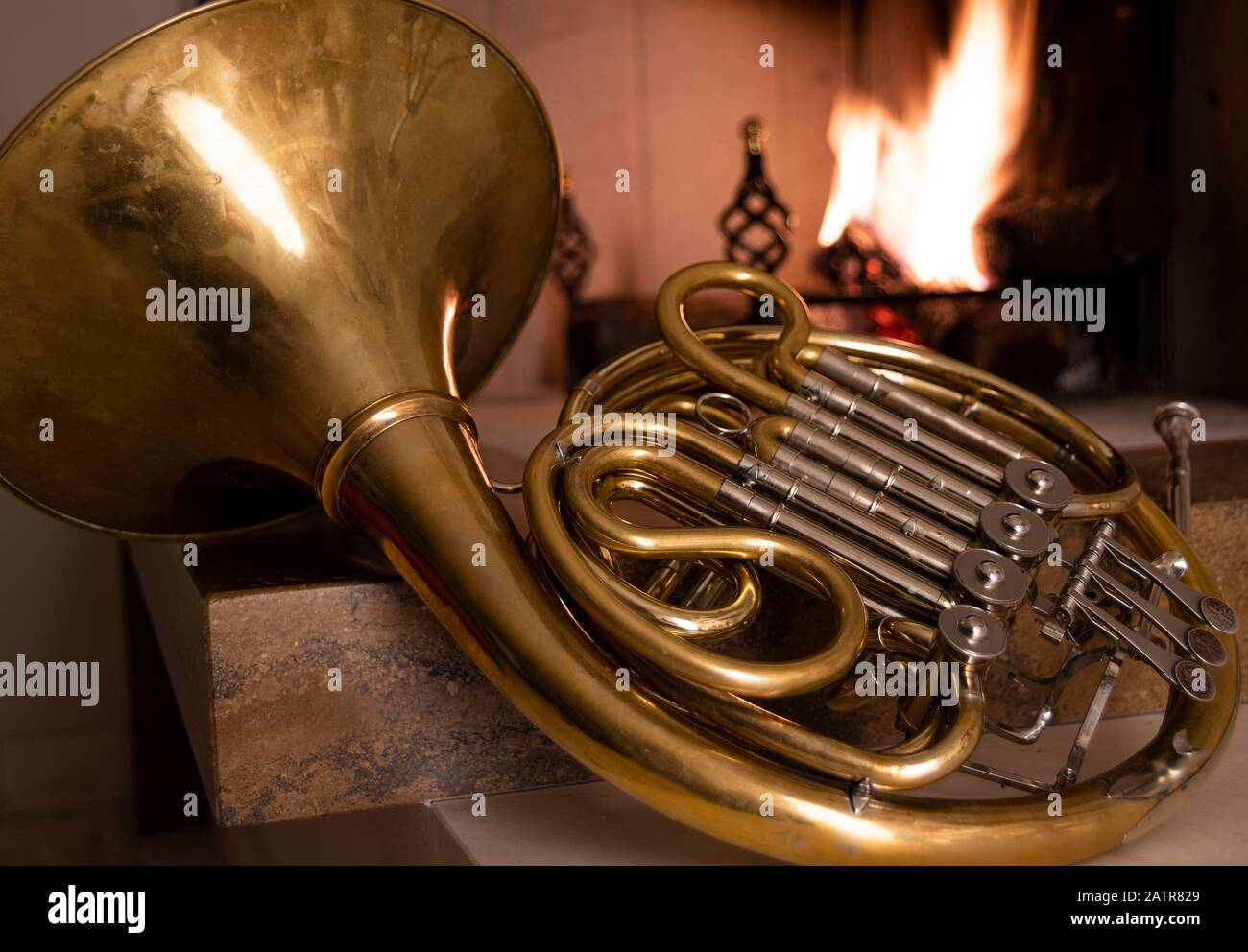 Close up on a French horn resting on a hearth in front of a burning ...