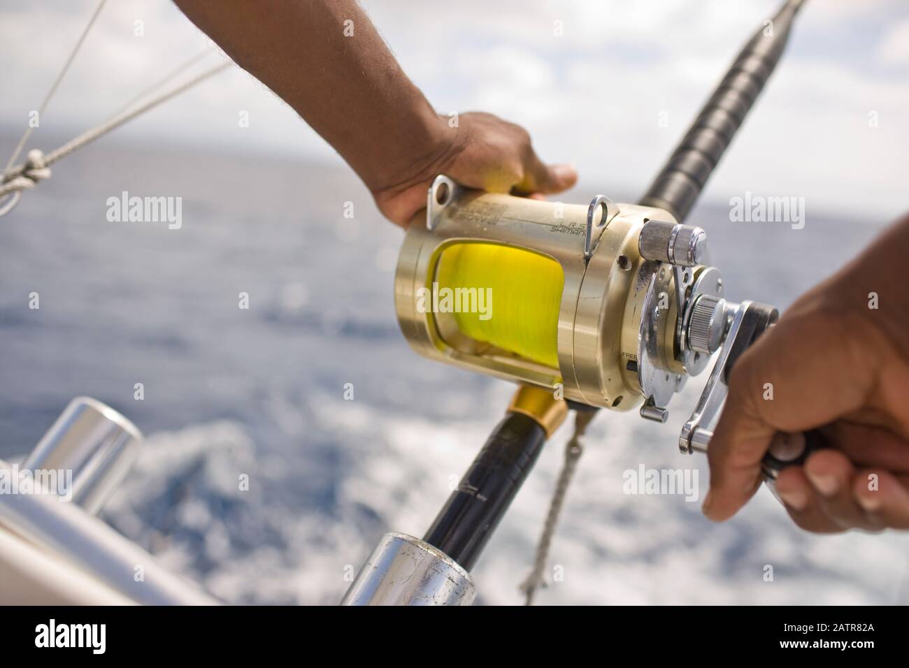 Man's hands reeling in a fishing line hanging off the side of a boat ...