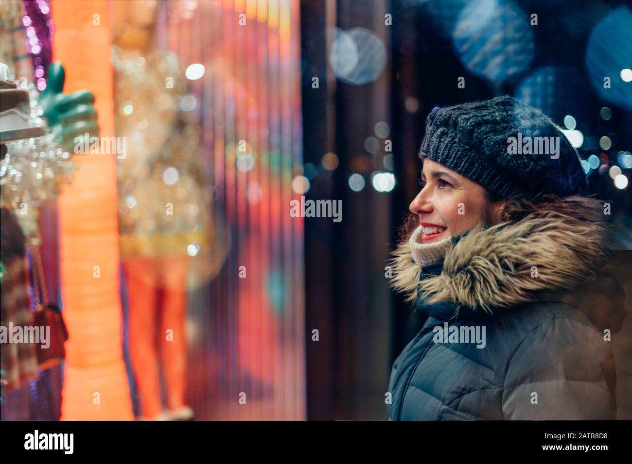 Beautiful girl looking at he showcase window on the night city street ...