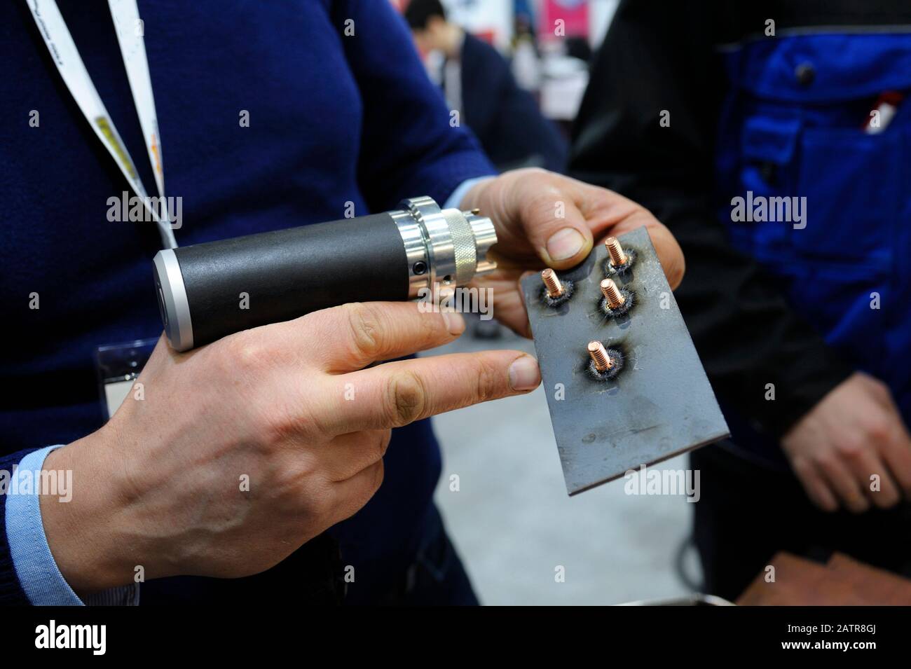 Worker hands hold the spot welding gun and screws welded to metal plate ...