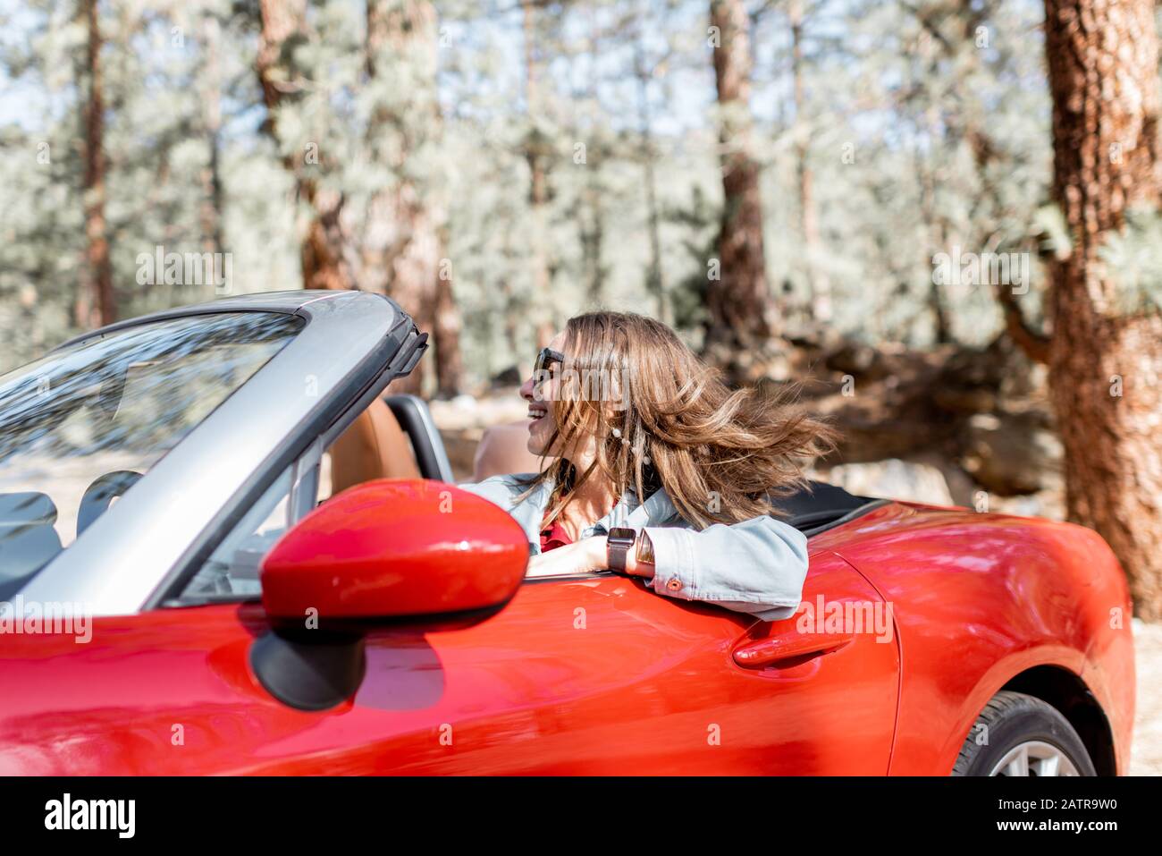 Portrait of a happy carefree woman driving convertible red car while ...
