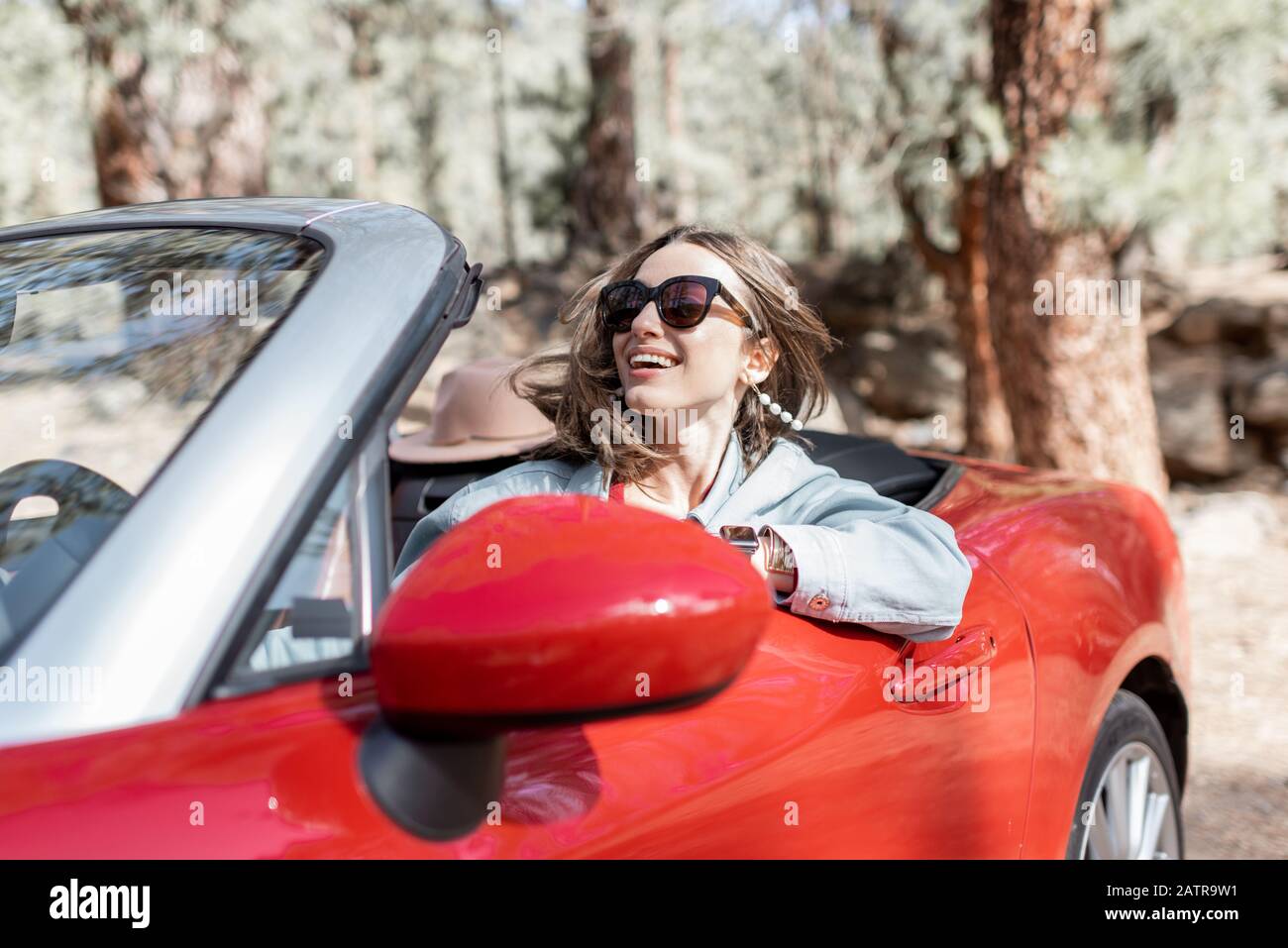 Portrait of a happy carefree woman driving convertible red car while ...