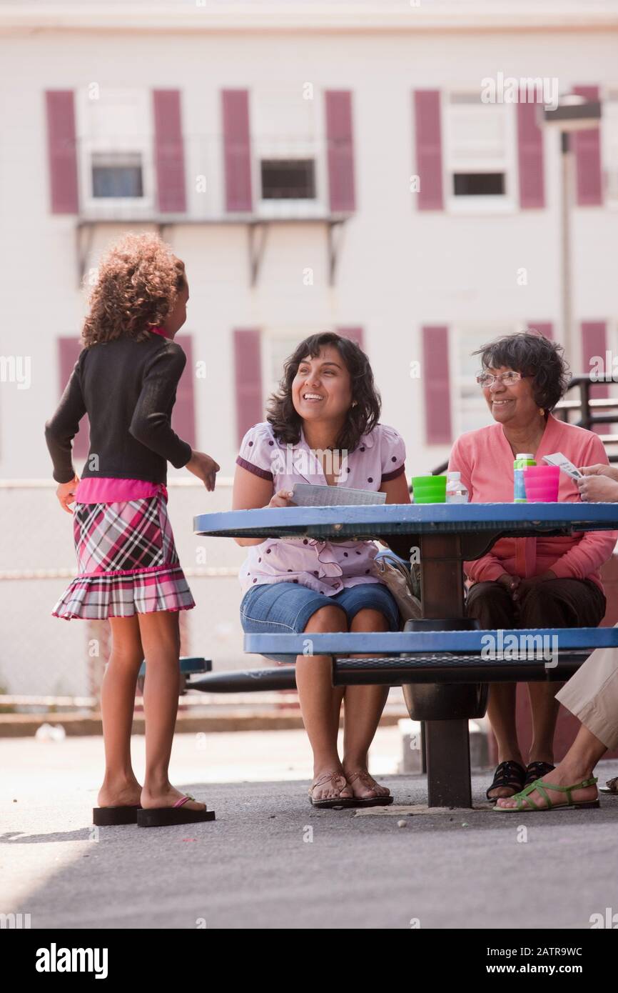 Girl stands talking to women who are sitting around a table outside ...