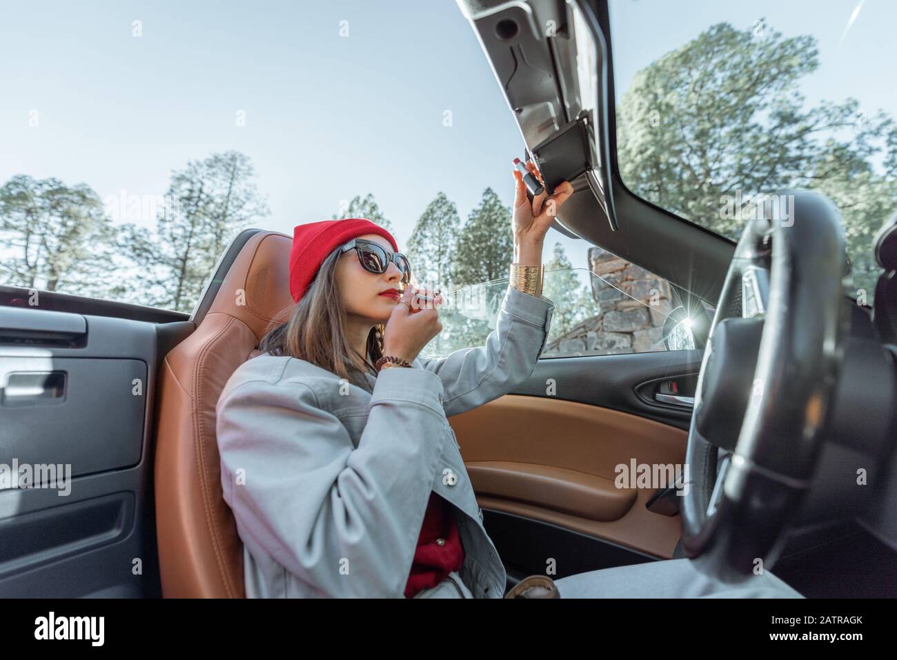 Woman applying makeup, drawing lips while sitting on the driver's seat ...