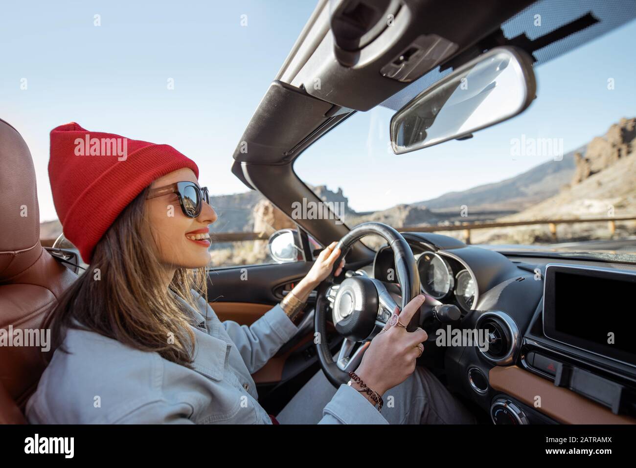 Happy woman in red hat driving convertible car while traveling on the ...