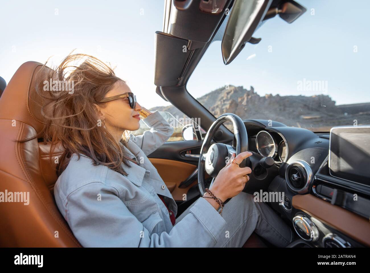Happy woman driving convertible car while traveling on the desert road ...