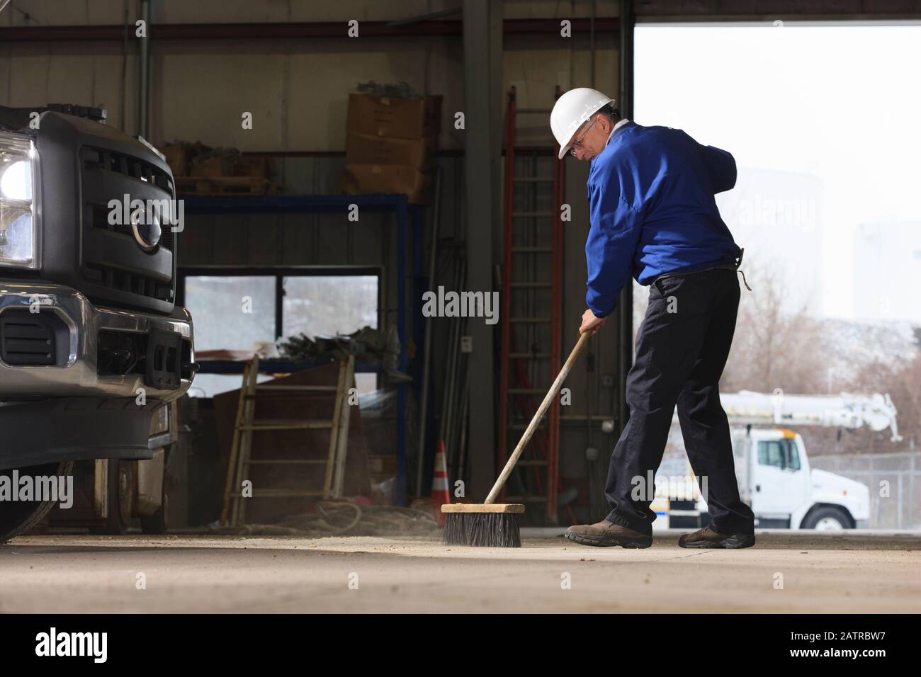 Man sweeping mechanic's workshop with a broom Stock Photo - Alamy