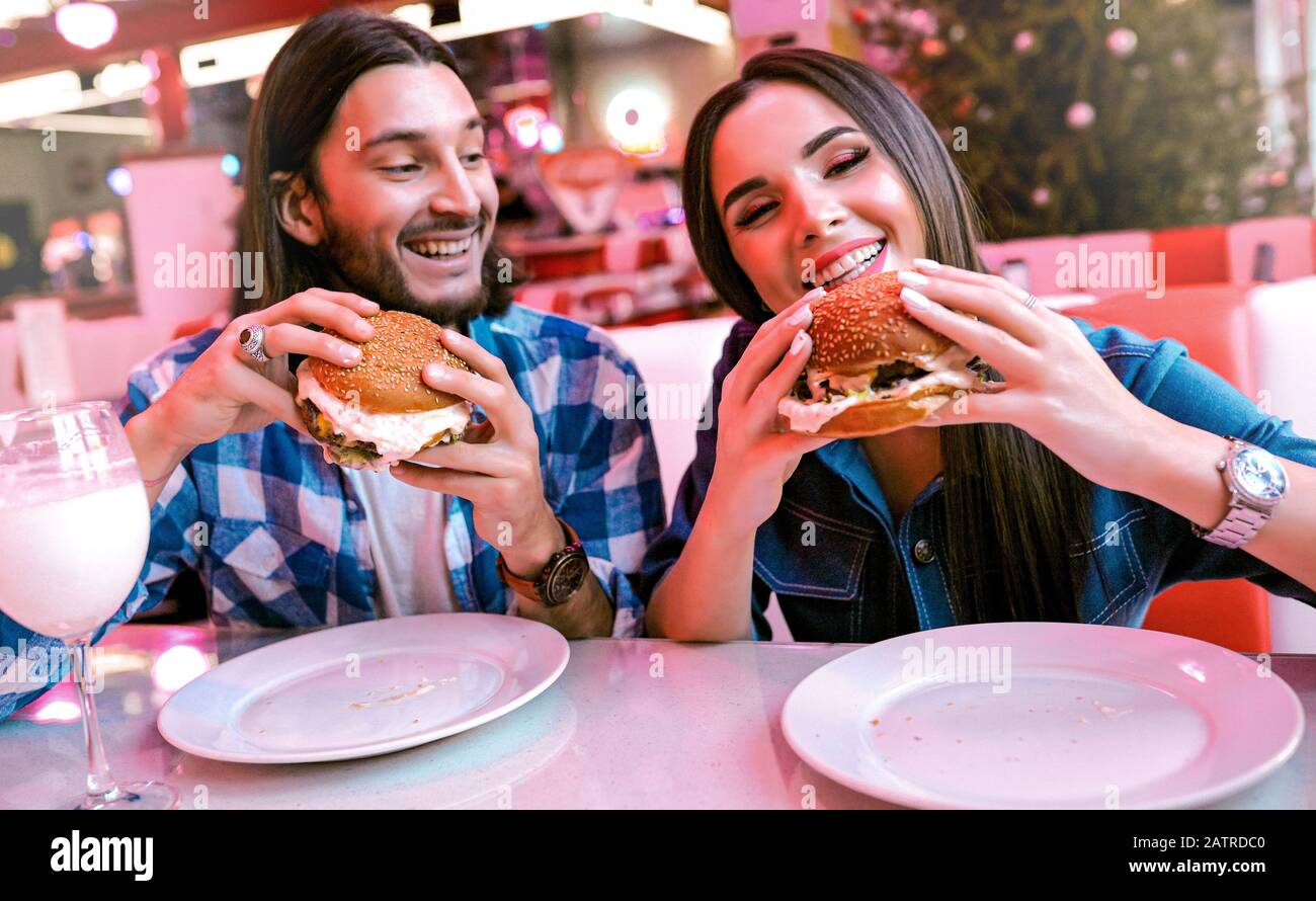 Couple in love having fun together, eating burgers in cafe and laughing ...