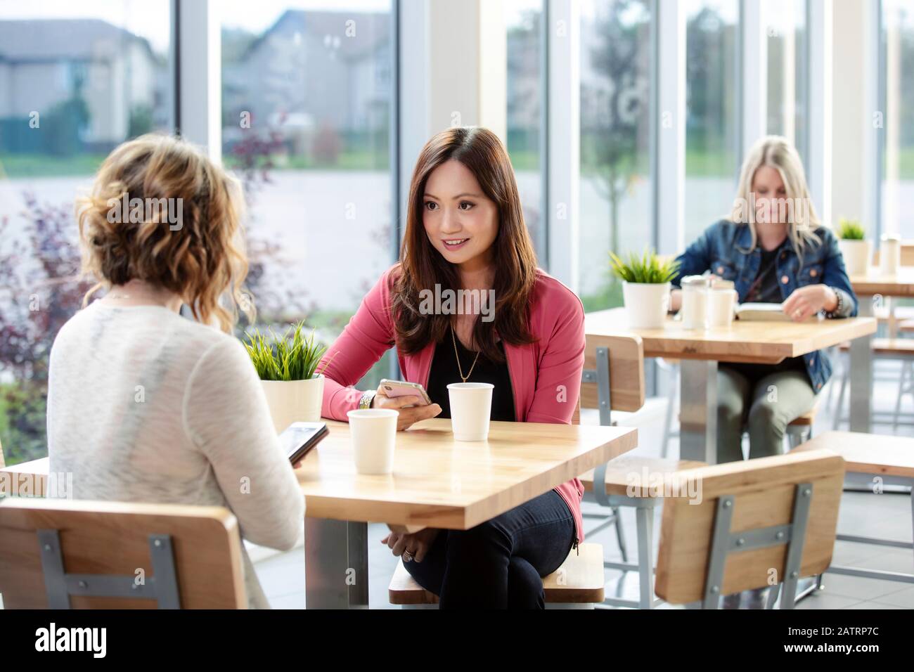 Two co-workers talking and checking their smart phones while another ...