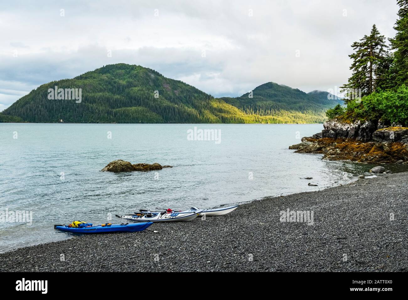 Three kayaks on the shoreline while late day light illuminates the ...