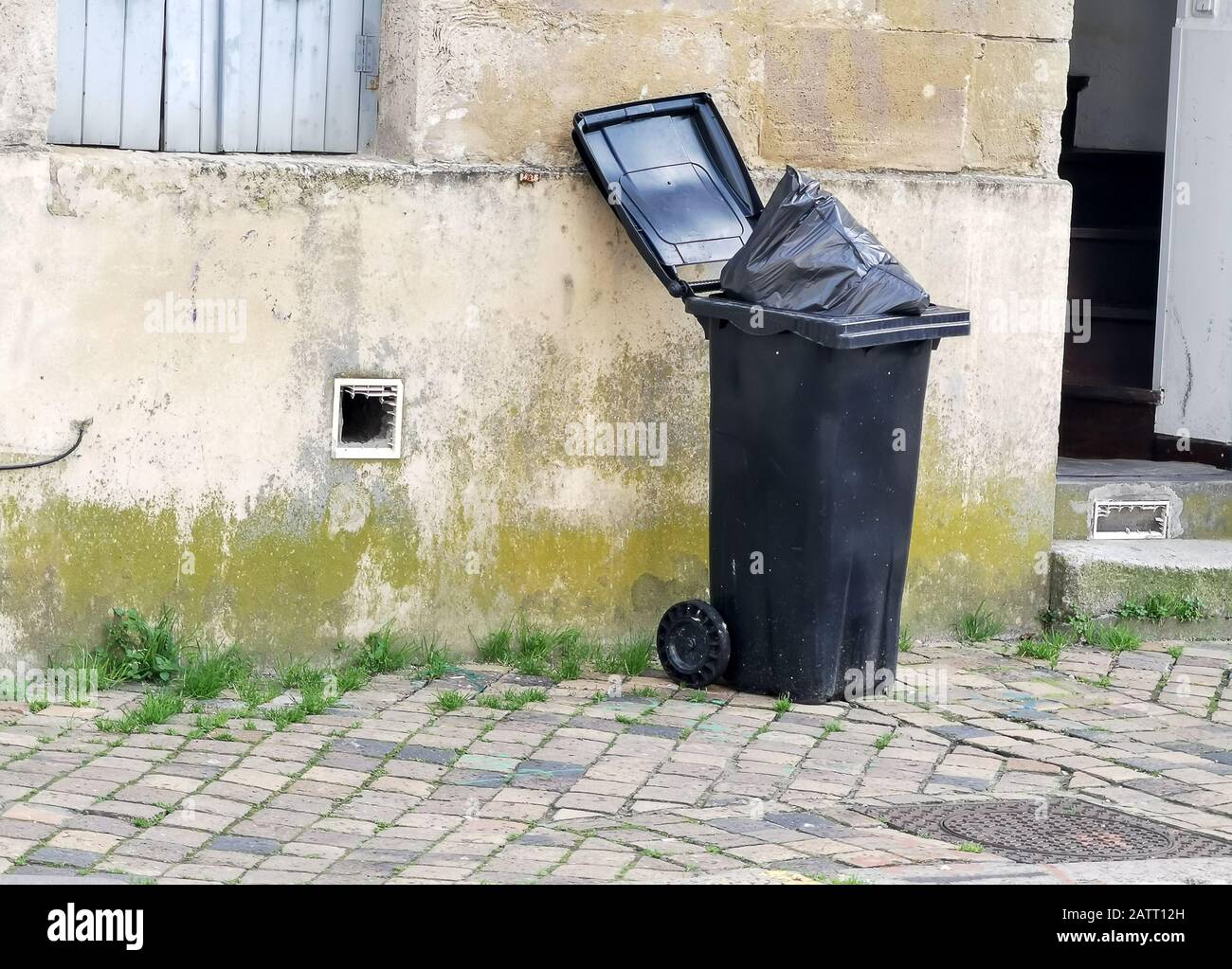Front door open and dark grey waste bin filled with garbage and plastic ...