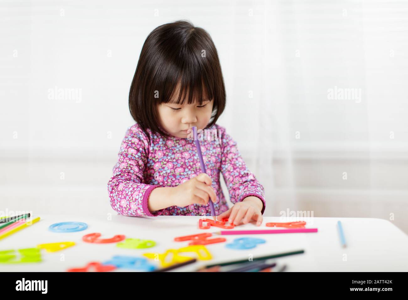 toddler girl practice writing letters on white paper against white ...