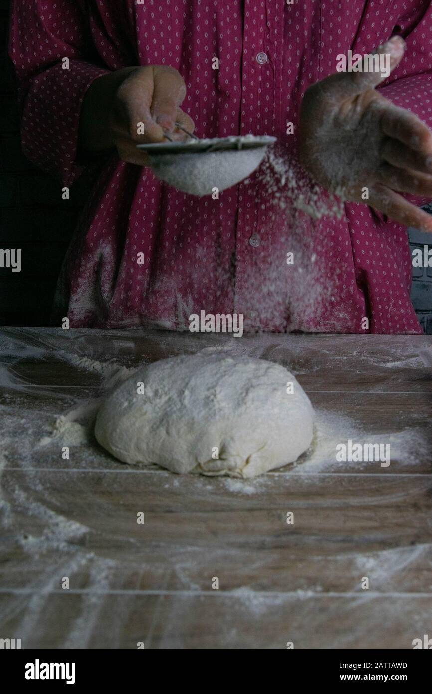 The woman sprinkles flour dough from the fullness for sifting flour ...
