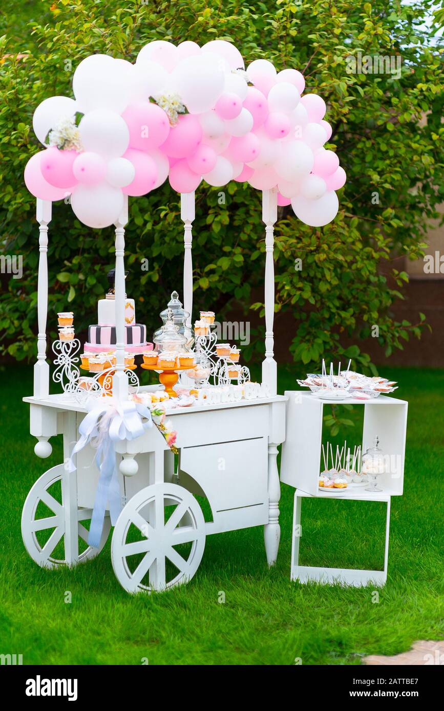 Candy Bar. White wooden trolley with sweets decorated with balloons on ...