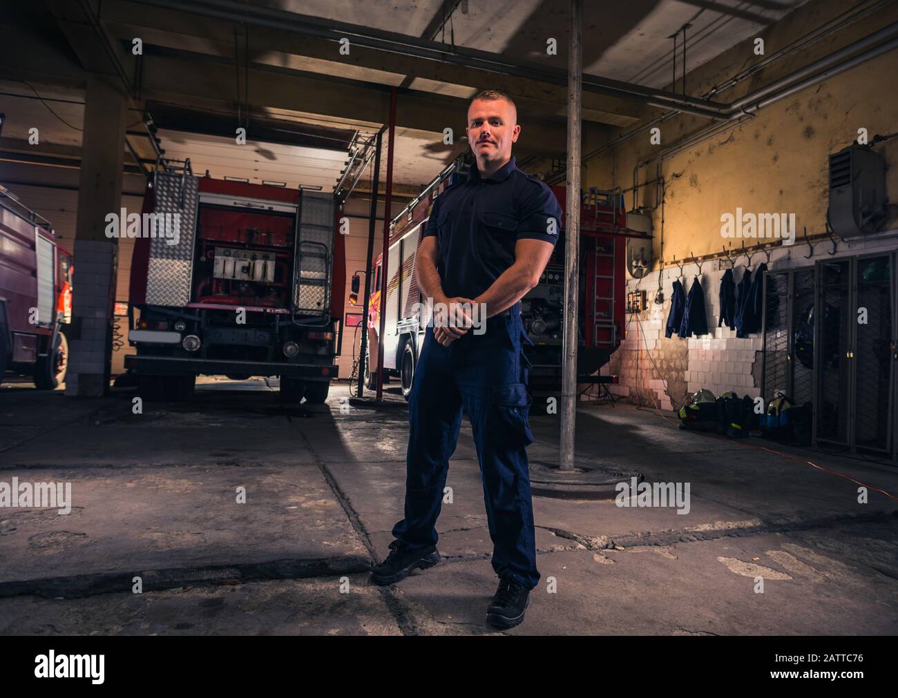 Portrait of handsome firefighter standing against trucks at fire ...