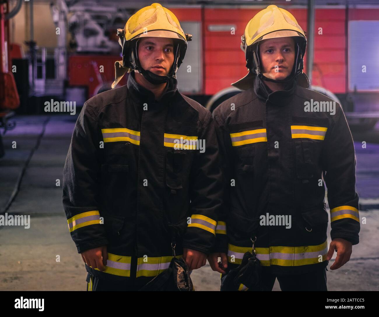 Portrait of two young firemen in uniform standing inside the fire ...