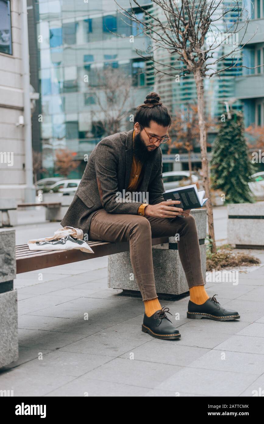 Modern day hipster reading a book at the city square during daytime ...