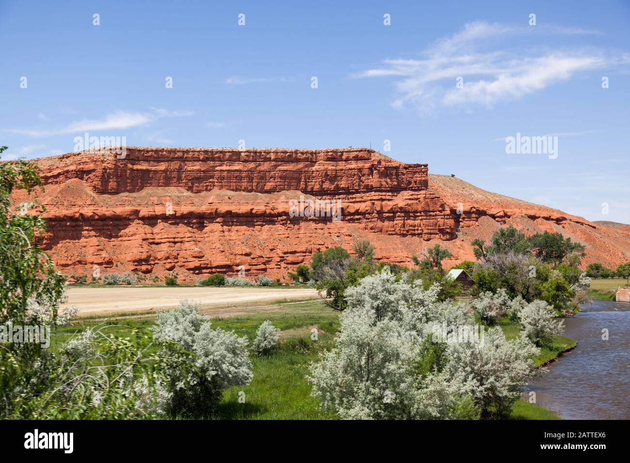 Red sedimentary rock that is eroding over time next to a patch of green ...