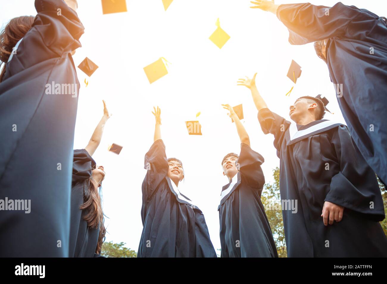 happy students in graduation gowns celebrating in university campus ...