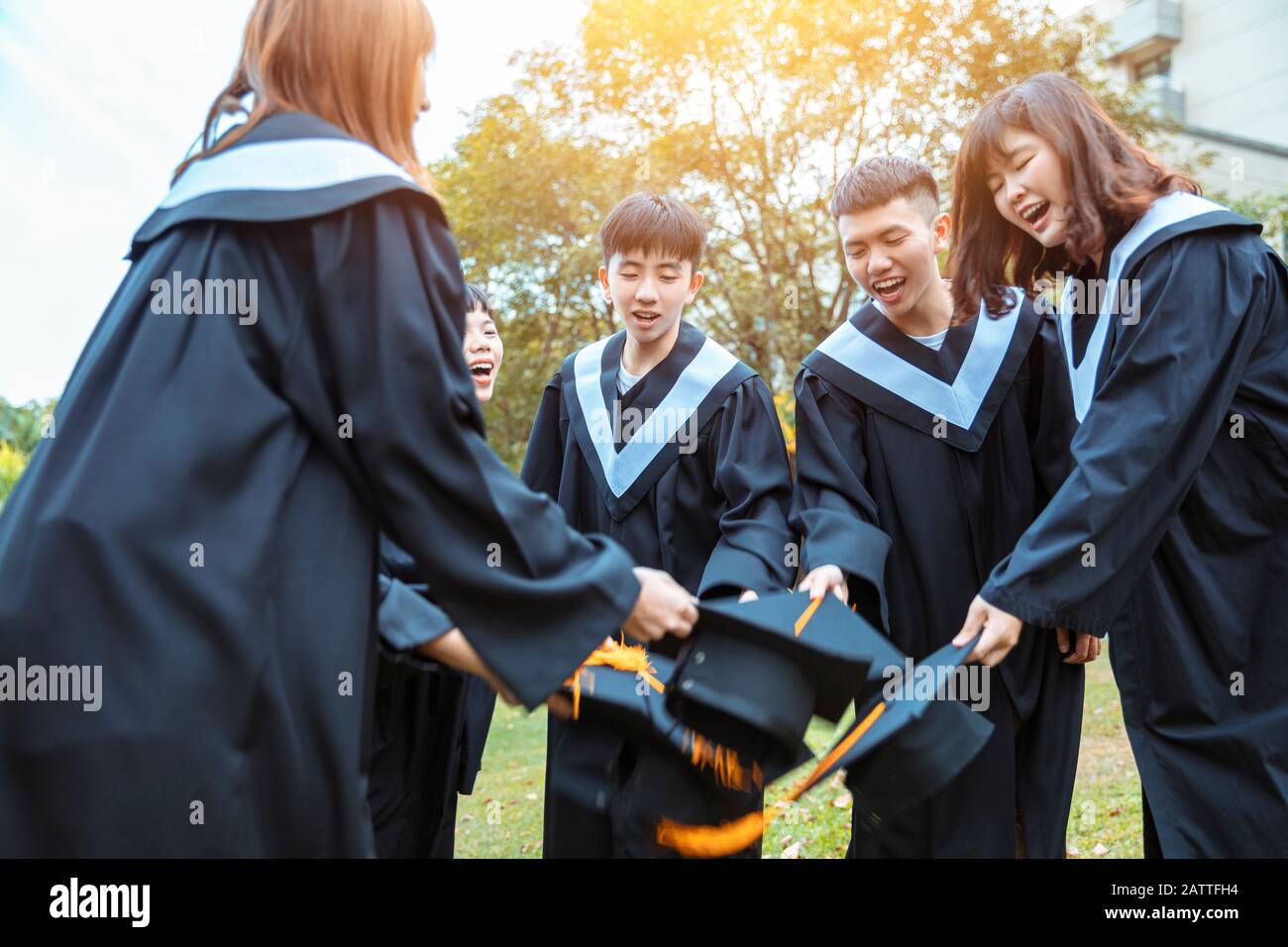 happy students in graduation gowns celebrating in university campus ...
