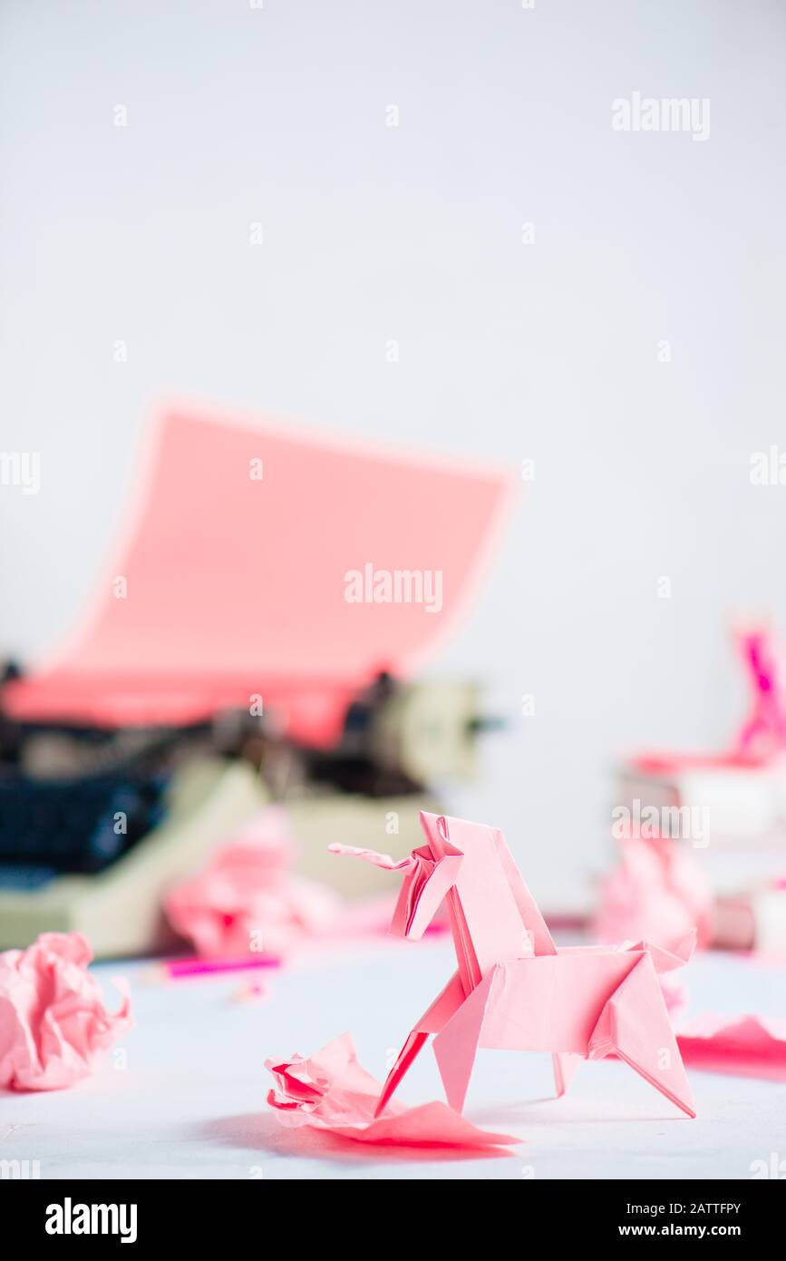 Pink origami unicorn with crumpled paper balls and a typewriter ...