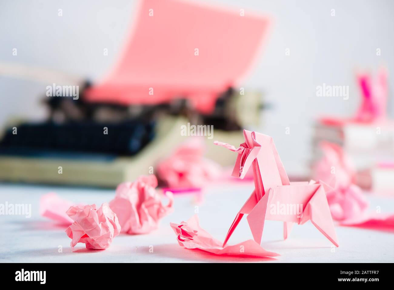 Pink origami unicorn with crumpled paper balls and a typewriter ...