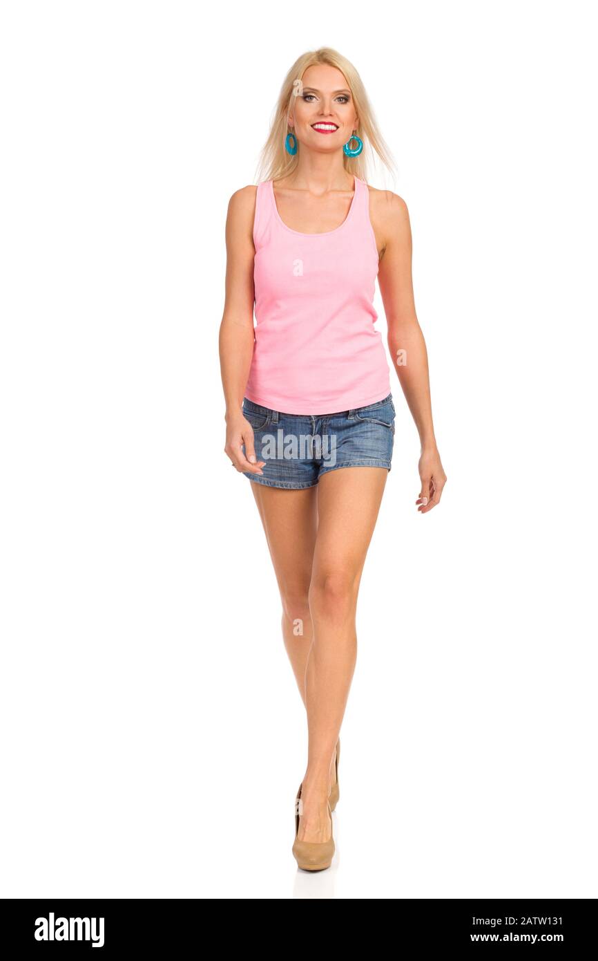 Beautiful blond woman in pink tank top, jeans shorts and high heels is ...