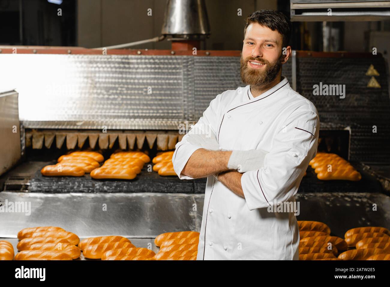 Portrait of a young baker on the background of an industrial oven in a ...