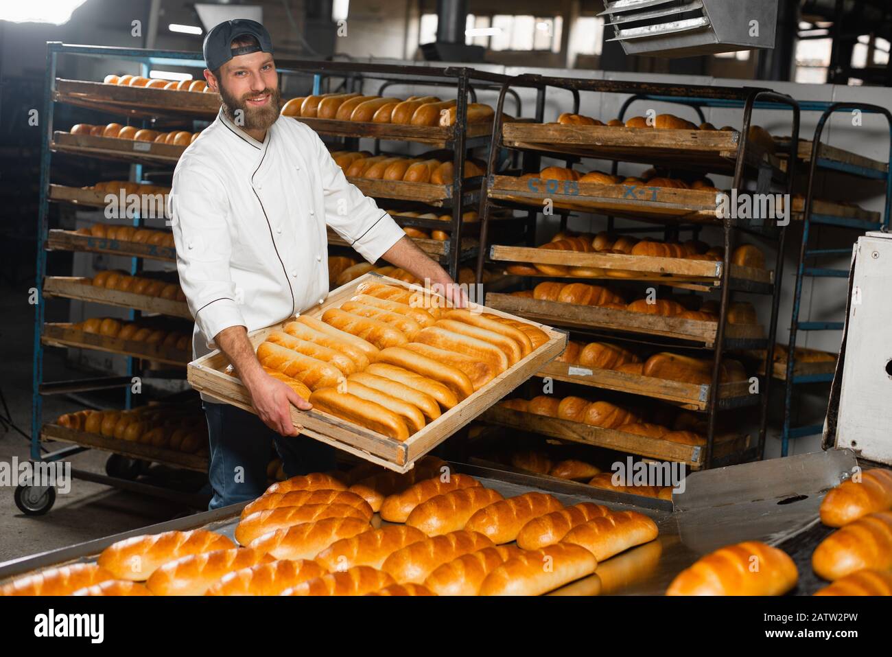 The baker holds a wooden box with hot bread on the background of ...