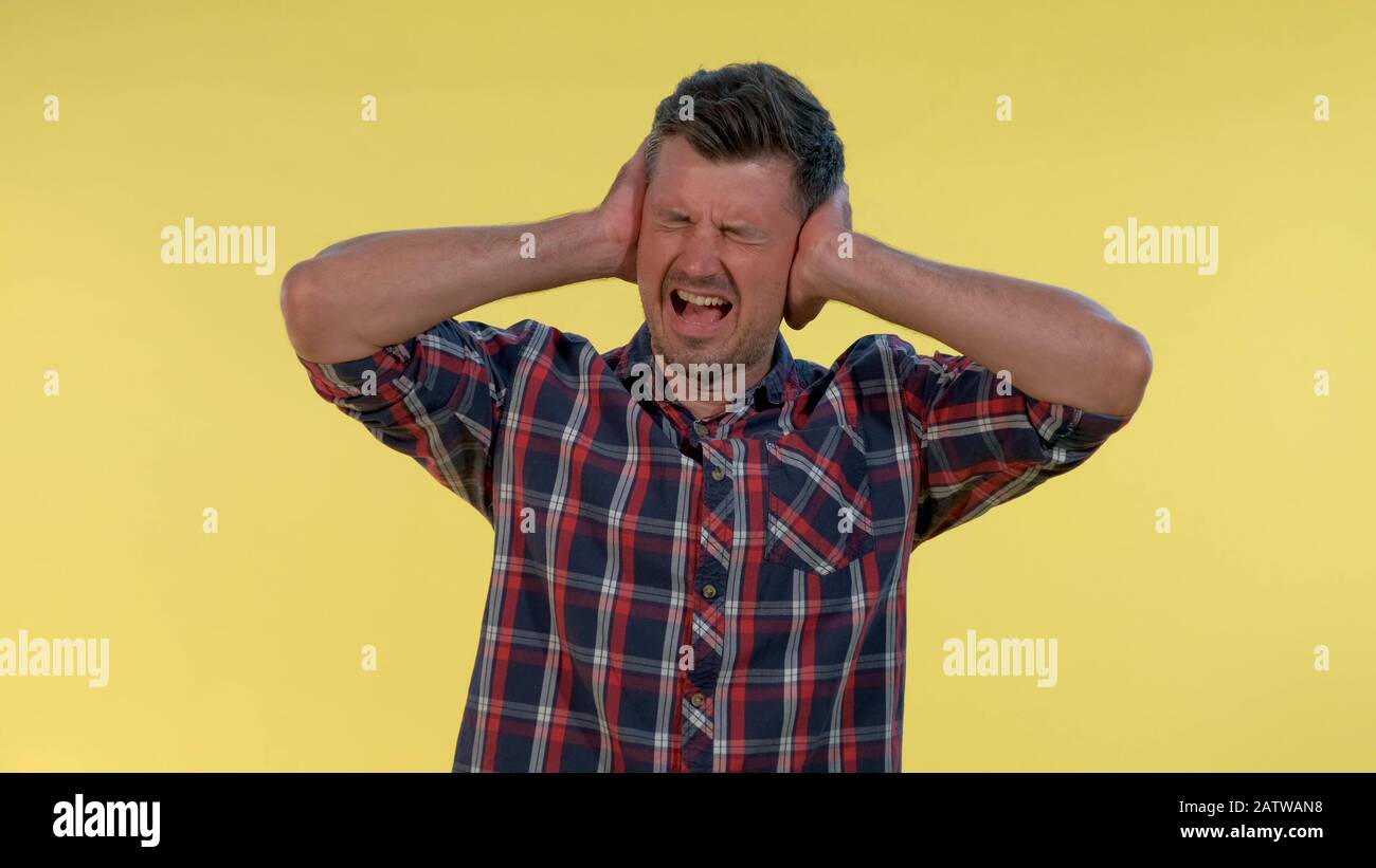 Scared desperate man screaming and covering ears on yellow background ...