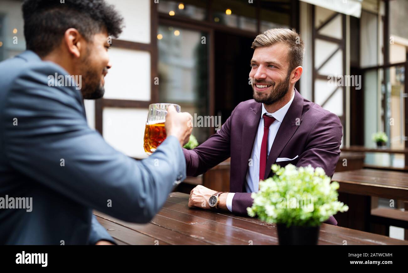 Having a pint with friend. Cheerful young men toasting with beer while ...